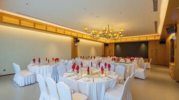 Uma sala de banquetes com várias mesas redondas, cadeiras brancas e guardanapos vermelhos.