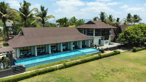 Um hotel moderno com piscina, área de estar coberta ao ar livre e palmeiras.