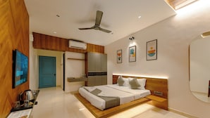 Um quarto de hotel moderno com uma cama, ventilador de teto, unidade de ar condicionado, piso de madeira, banheiro com espelho e obras de arte nas paredes.