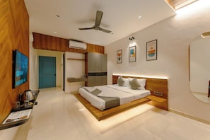 Um quarto de hotel moderno com uma cama, ventilador de teto, unidade de ar condicionado, piso de madeira, banheiro com espelho e obras de arte nas paredes.
