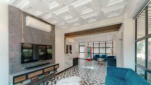 Um lobby moderno com uma televisão grande, lareira de mármore, piso com padrão geométrico e assentos azuis.