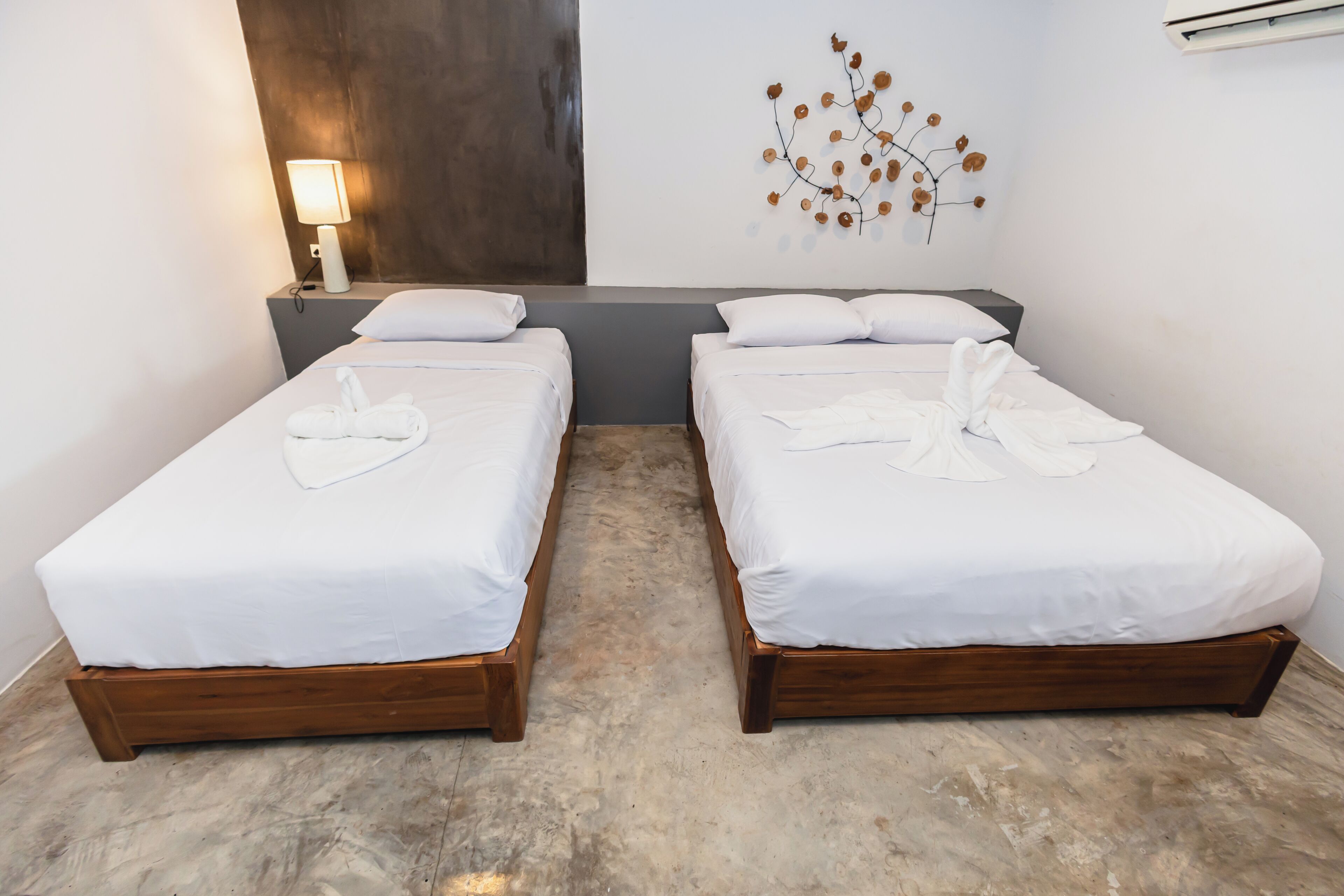 Quarto de hotel com duas camas, ar condicionado fixado na parede, um objeto decorativo na parede e um abajur.