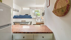 Cozinha com bancada de mármore, área de refeições com mesa e cadeiras, sofá e uma grande cesta de vime na parede.
