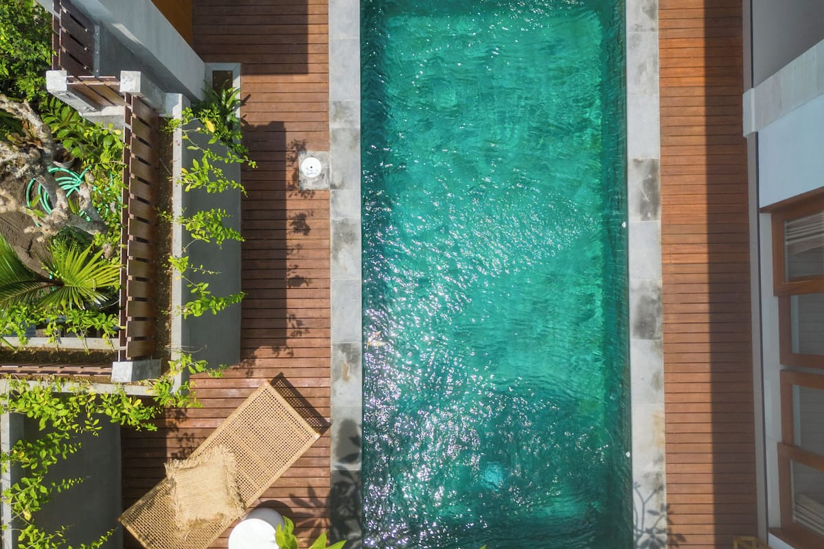 Piscina no terraço com água cristalina, rodeada por um deck de madeira e vegetação exuberante.