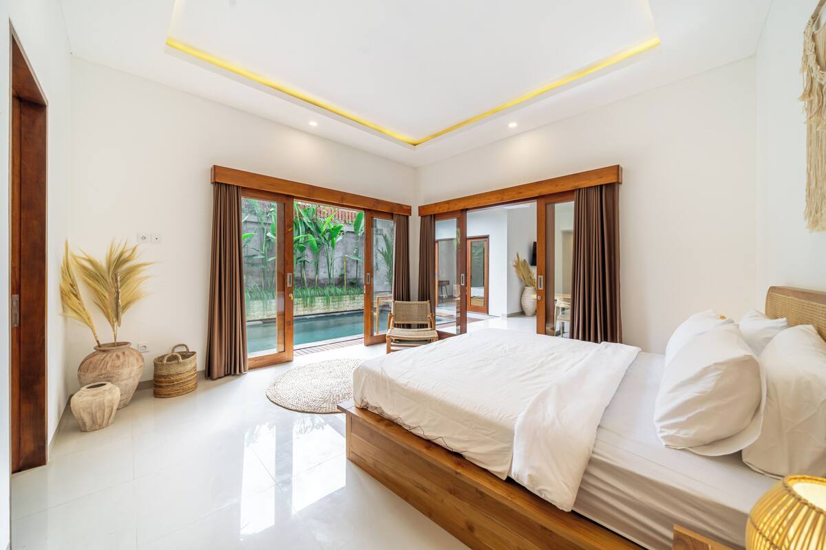 Quarto moderno com uma cama grande, portas de vidro deslizantes para uma piscina e vista para o verde.