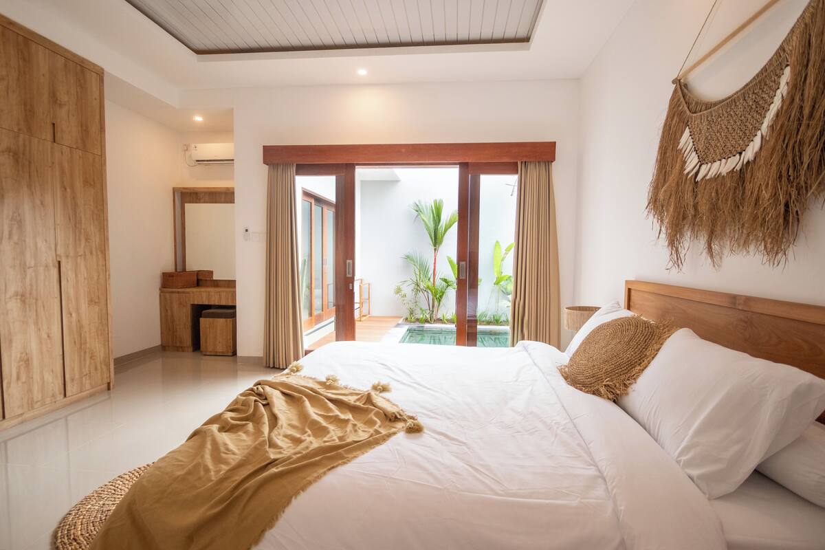 Quarto com uma cama grande, guarda-roupa de madeira e vista para uma piscina e áreas verdes.