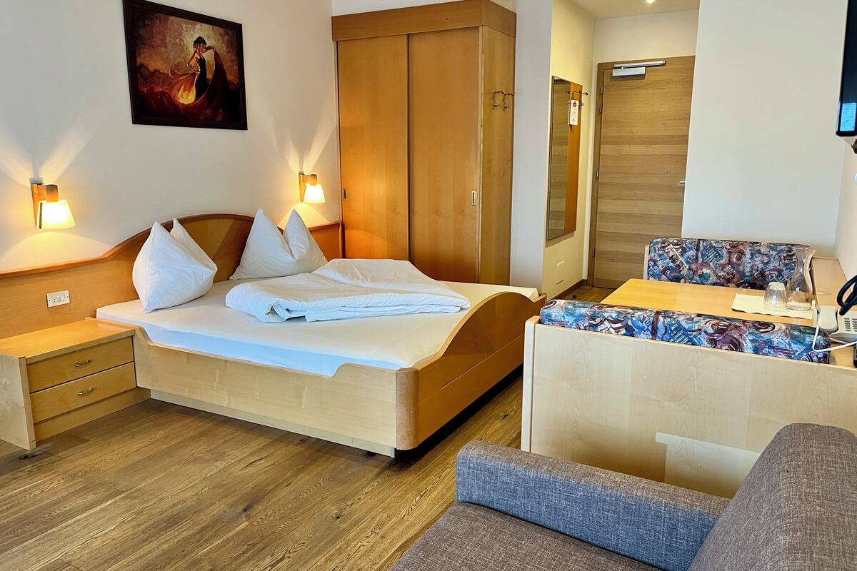 Quarto de hotel com cama, mesas de cabeceira, escrivaninha com cadeira, guarda-roupa e um quadro na parede.
