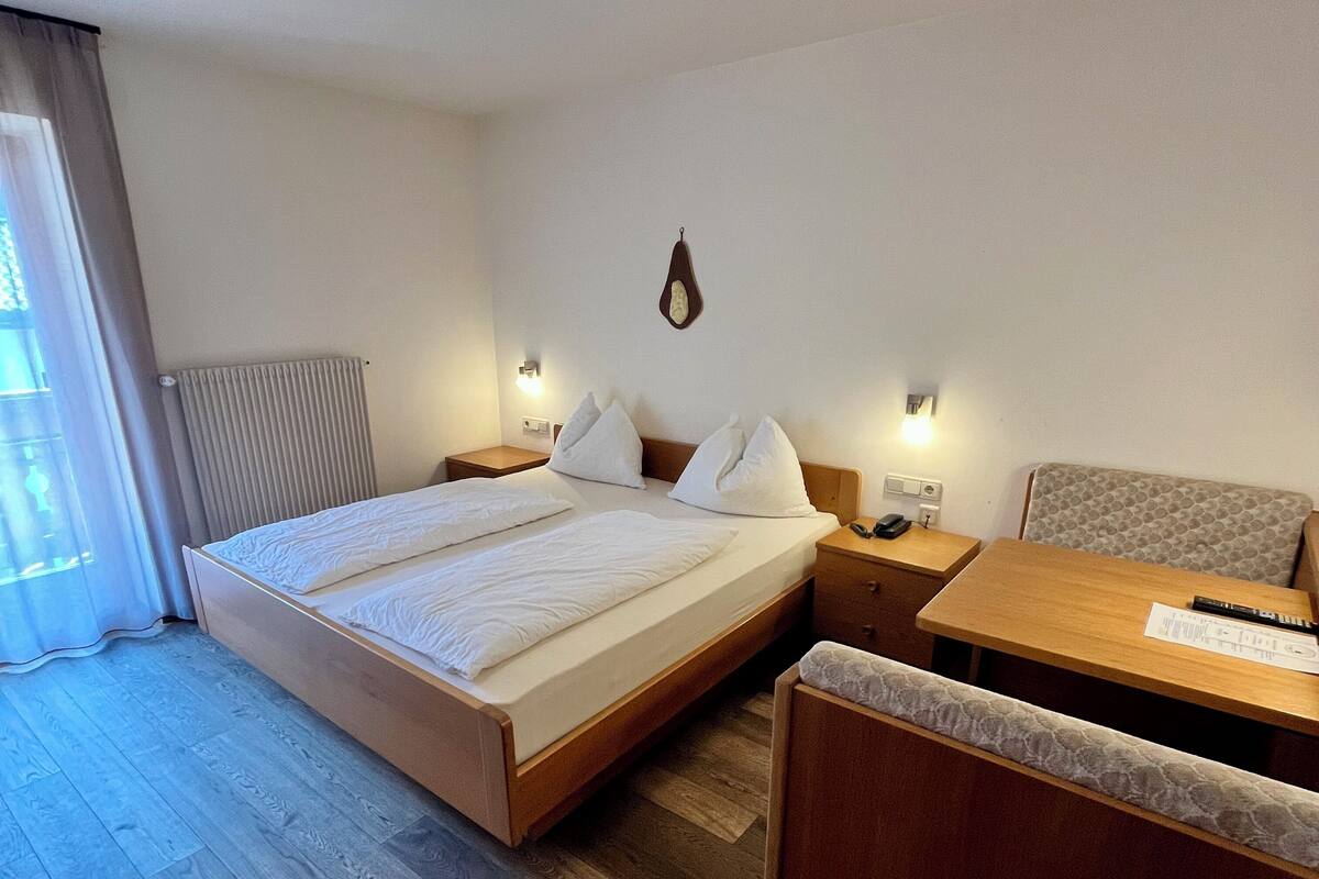 Quarto de hotel com cama, mesas de cabeceira, escrivaninha e uma cadeira.