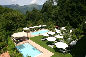 Uma área de piscina com várias espreguiçadeiras e guarda-sóis, rodeada por vegetação exuberante e montanhas ao fundo.