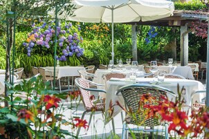 Uma área de refeições ao ar livre com mesas e cadeiras, rodeada por vegetação exuberante e flores.