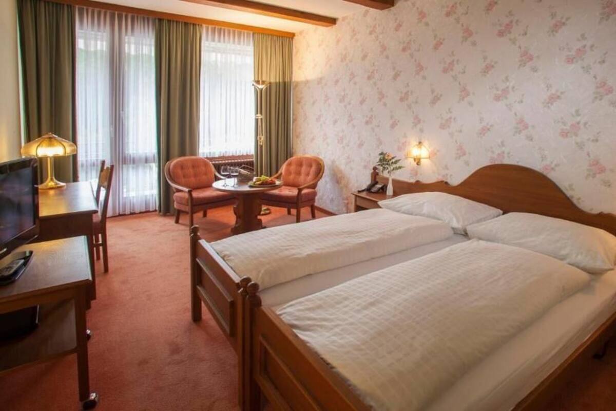 Quarto de hotel com cama de casal, escrivaninha com luminária, cadeira, mesinha com frutas e televisão.