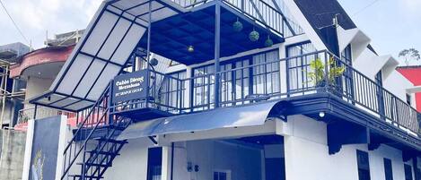 Um edifício moderno com varanda, escadaria e uma placa indicando que é uma pensão.