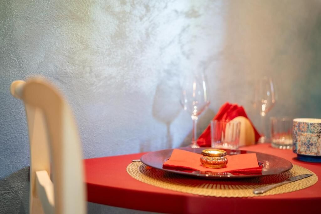 Mesa de jantar com toalha vermelha, peça central dourada e cadeira branca.