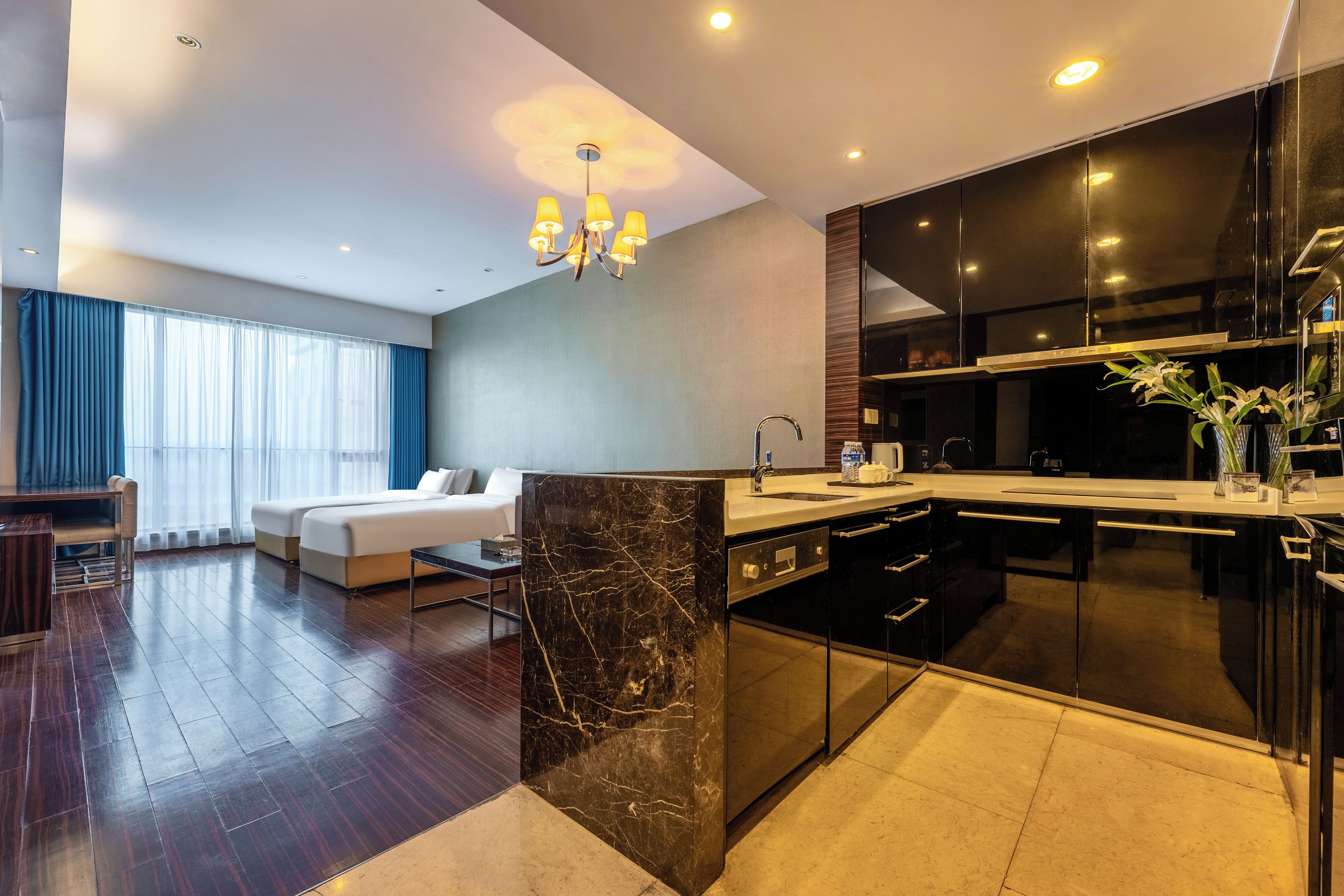 Quarto de hotel moderno com uma cama grande, área de jantar e cozinha com bancada de mármore.