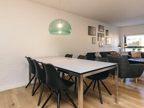 Uma sala de jantar moderna com uma mesa branca, cadeiras pretas e uma luminária pendente verde.