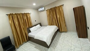 Quarto com cama, cortinas, ar condicionado e uma cadeira.