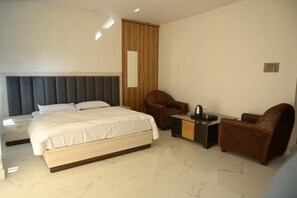 Quarto de hotel com cama, mesa de cabeceira, cadeira, pequena mesa e guarda-roupa.