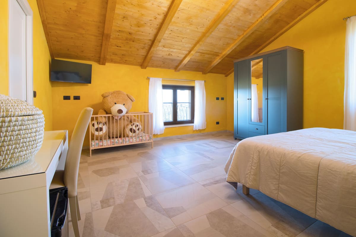 Quarto com cama, berço, guarda-roupa e televisão na parede.