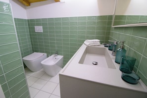 Casa de banho com azulejos verdes, uma sanita branca, dois sanitas e um espelho.
