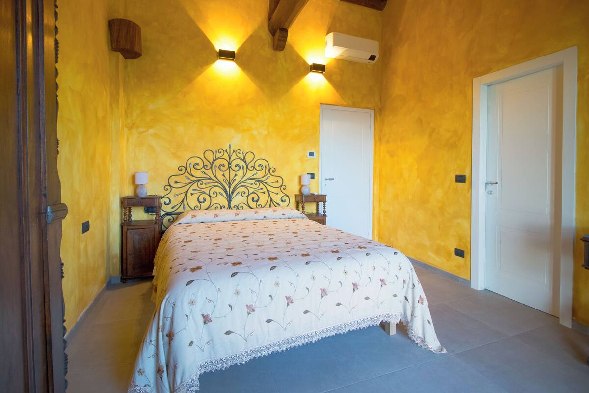 Quarto com cama, mesas de cabeceira, cabeceira decorativa e porta.