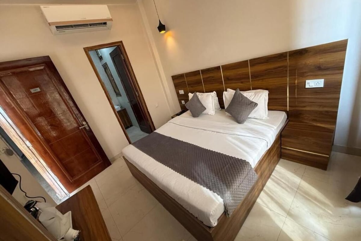 Quarto de hotel com cabeceira de madeira, cama com roupa de cama branca e cinza, manta cinza e guarda-roupa de madeira.