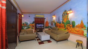 Uma sala de estar com dois sofás, uma mesa de centro, uma televisão e um mural na parede.