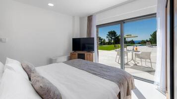 Quarto com cama, TV sobre suporte de madeira e varanda com mobiliário externo.