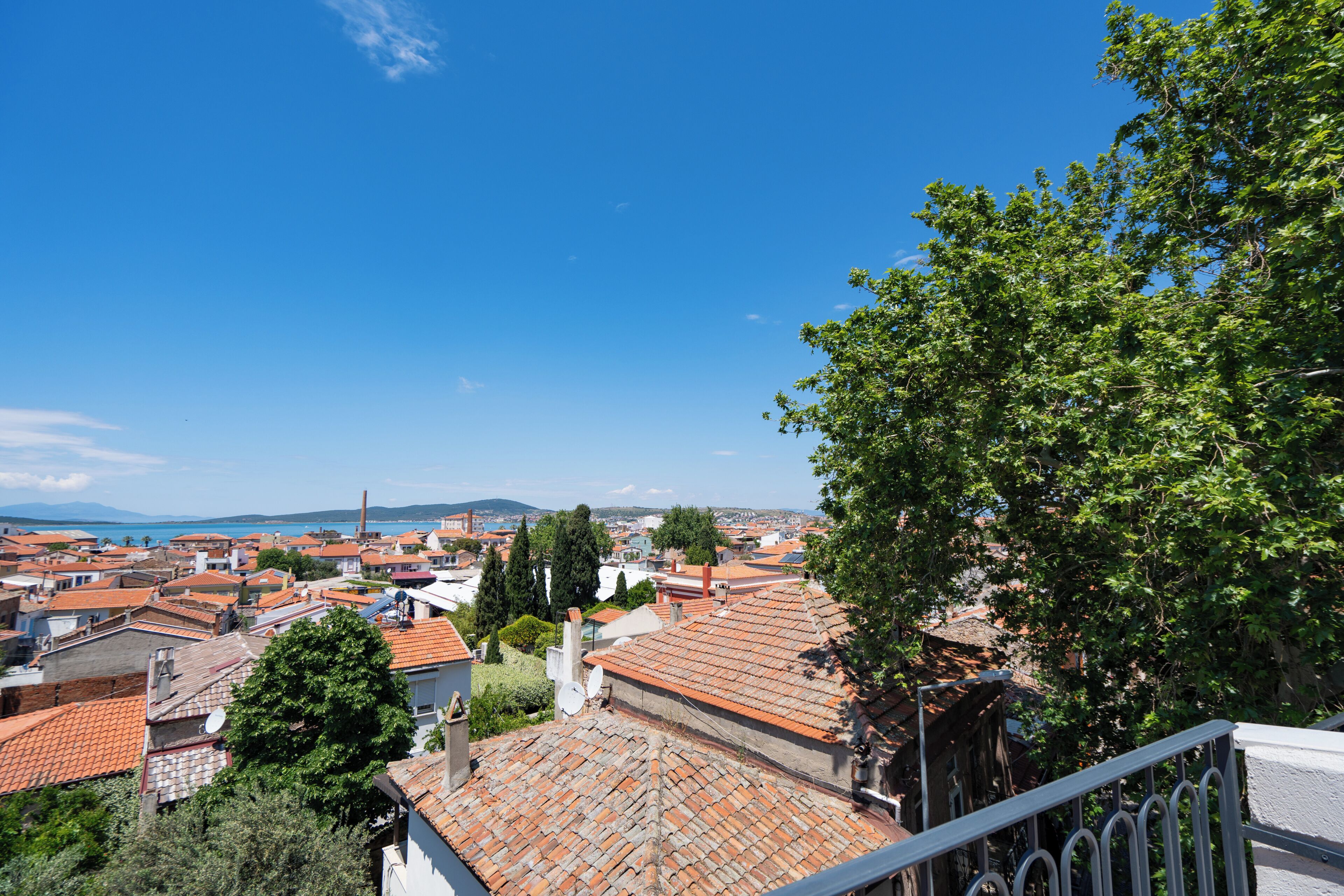 Paisagem urbana com telhados de telhas vermelhas, árvores verdes e céu azul claro.