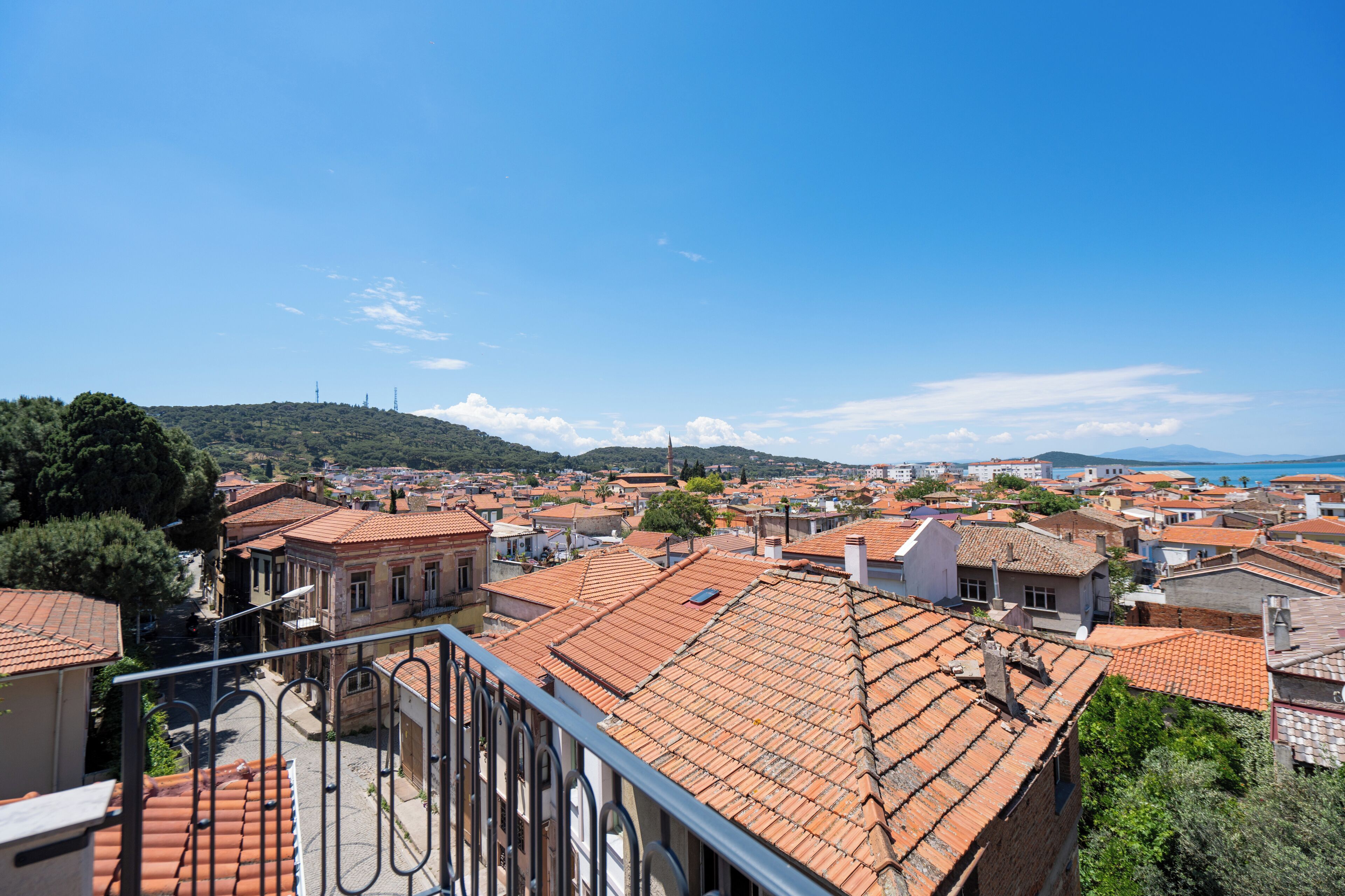 Vista de edifícios com telhados de terracota, céu azul límpido e colinas ao longe.