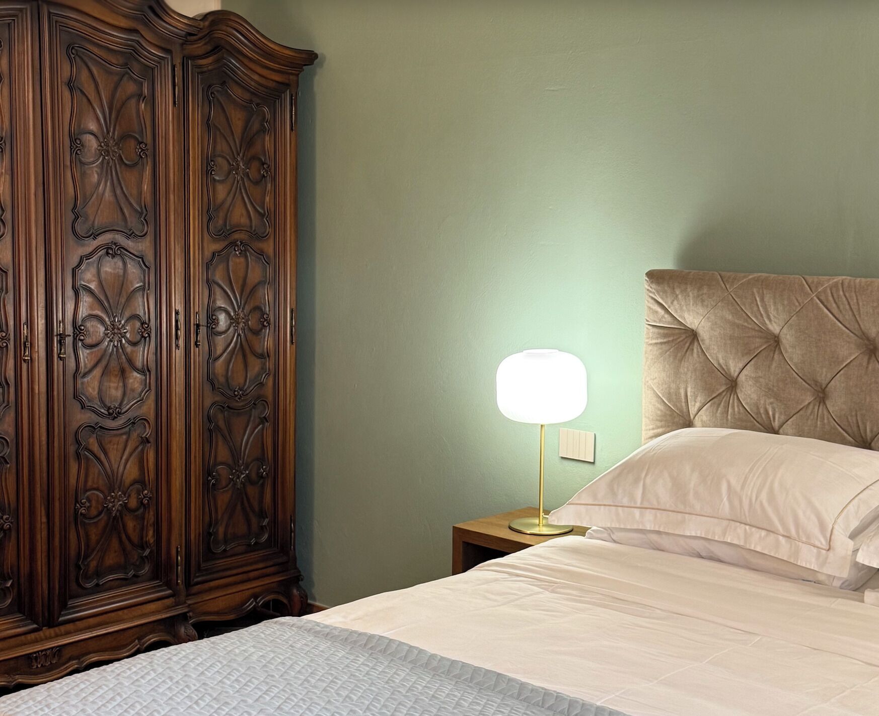 Quarto com um armário de madeira grande, luminária de cabeceira, cama com cabeceira estofada e mesa de cabeceira com um bloco de notas.