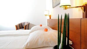 Quarto de hotel com duas camas, uma cadeira, um abajur e um vaso de planta.