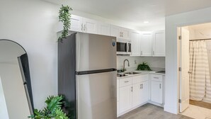 Uma cozinha moderna com armários brancos, uma geladeira de aço inoxidável, um micro-ondas e uma pia.