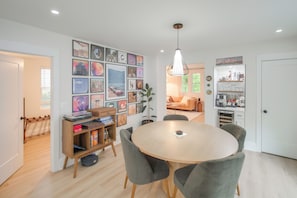 Uma sala de jantar moderna com uma mesa redonda, cadeiras cinzentas e uma parede decorada com fotografias emolduradas.