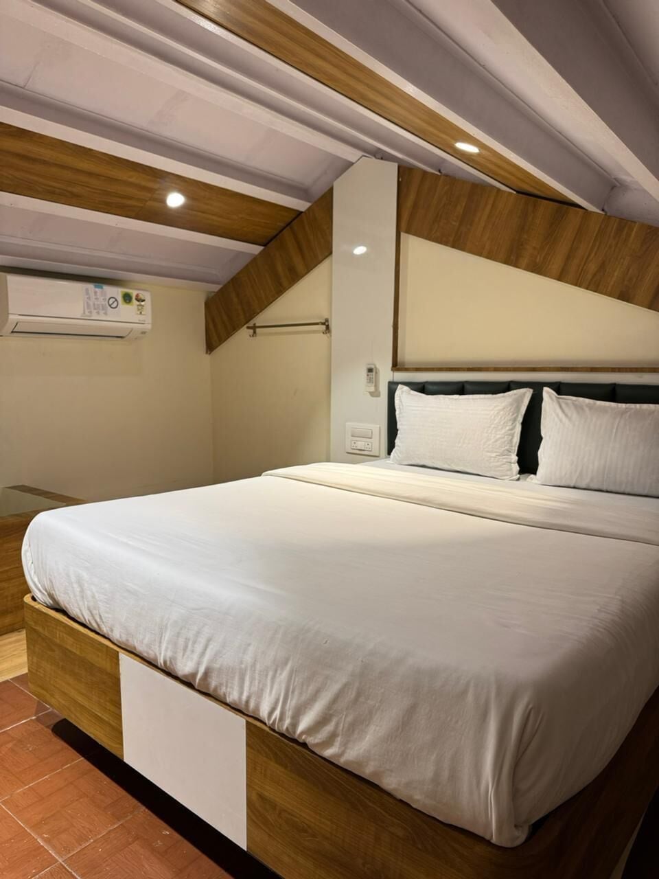 Quarto com cabeceira de madeira, colcha branca e compartimento de armazenamento embutido sob a cama.
