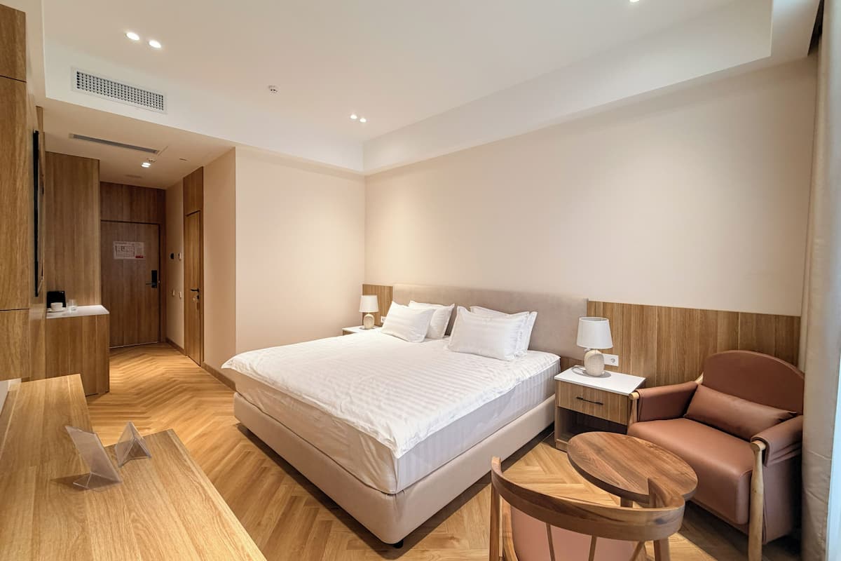 Quarto de hotel com uma cama grande, mesas de cabeceira, escrivaninha, cadeira e guarda-roupa.