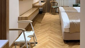 Quarto de hotel com cama, escrivaninha, cadeira, televisão na parede e janela com cortinas.