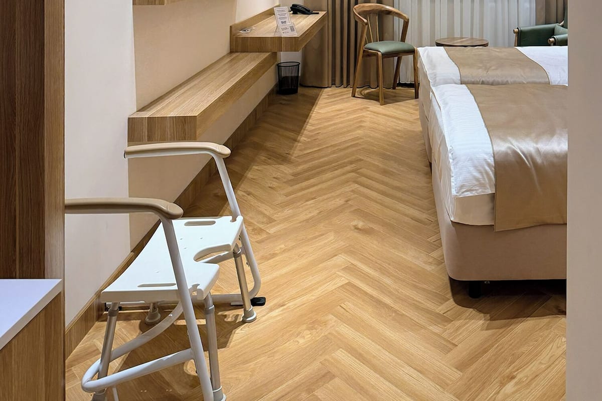 Quarto de hotel com cama, escrivaninha, cadeira, televisão na parede e janela com cortinas.