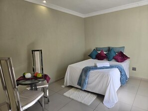 Quarto com cama, cadeira, mesinha e espelho.