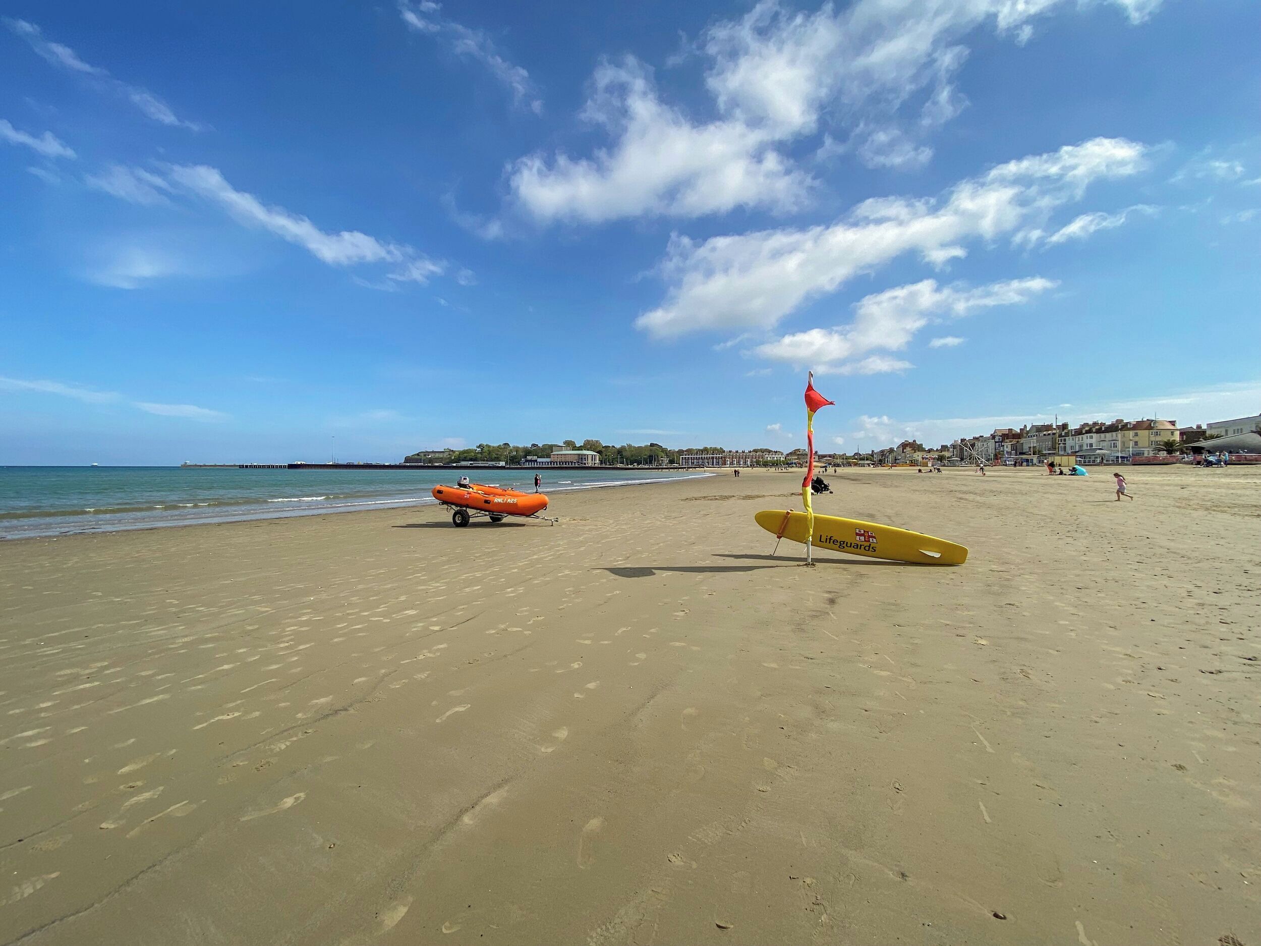 Uma praia com equipamentos de salva-vidas, incluindo uma bandeira vermelha e uma prancha de surf amarela.