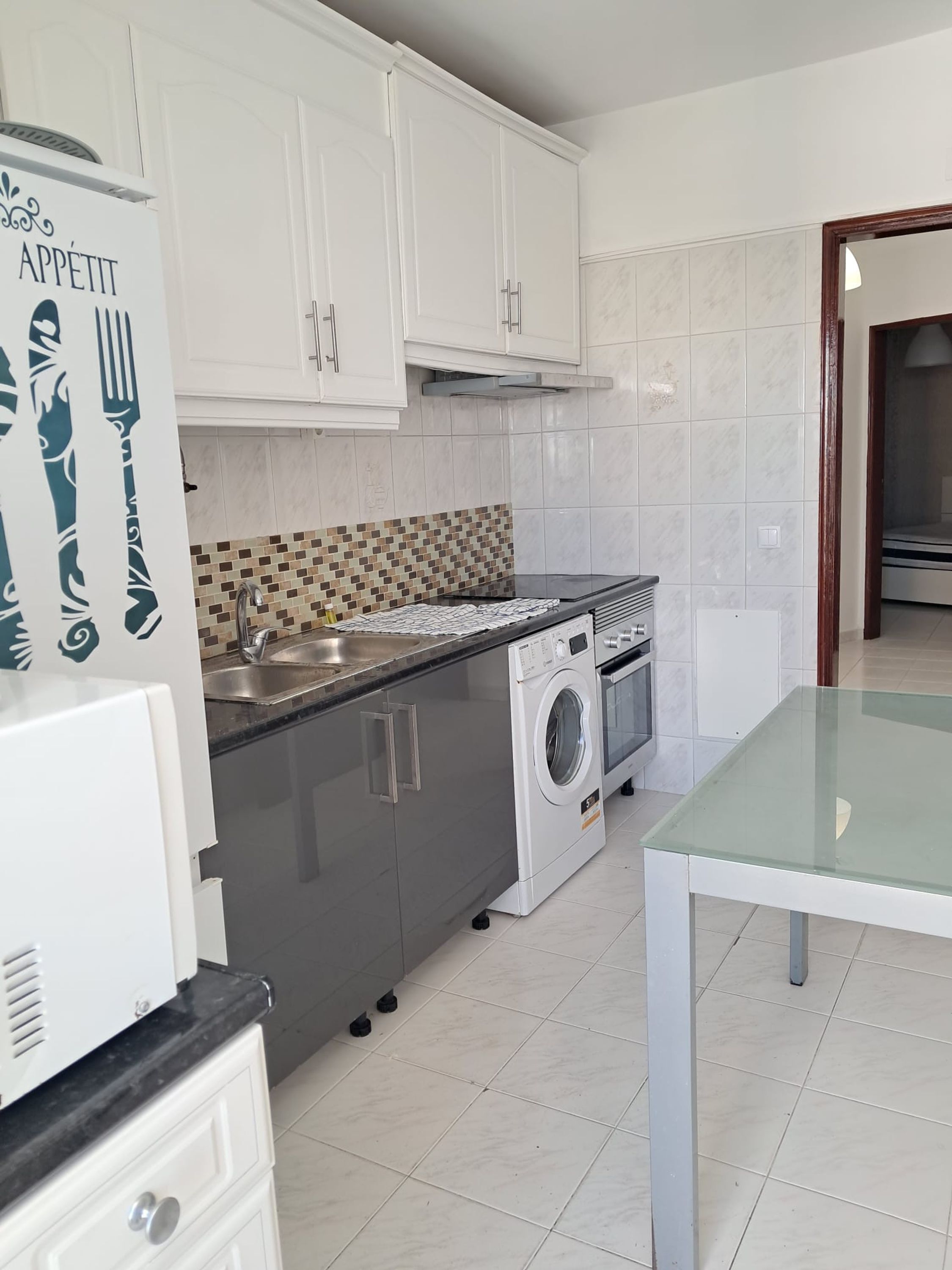 Uma cozinha compacta com máquina de lavar, pia e mesa de jantar.