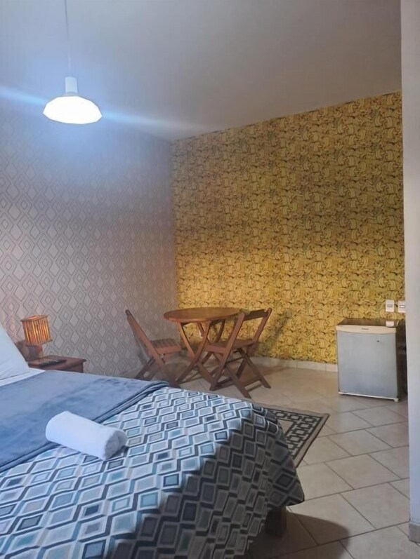 Quarto com cama, mesa, cadeiras, um pequeno armário e papel de parede estampado.