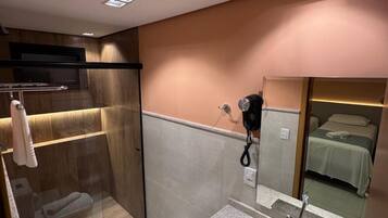 Uma casa de banho moderna com cabine de duche em vidro, sanita, lavatório com espelho e secador de cabelo fixado na parede.