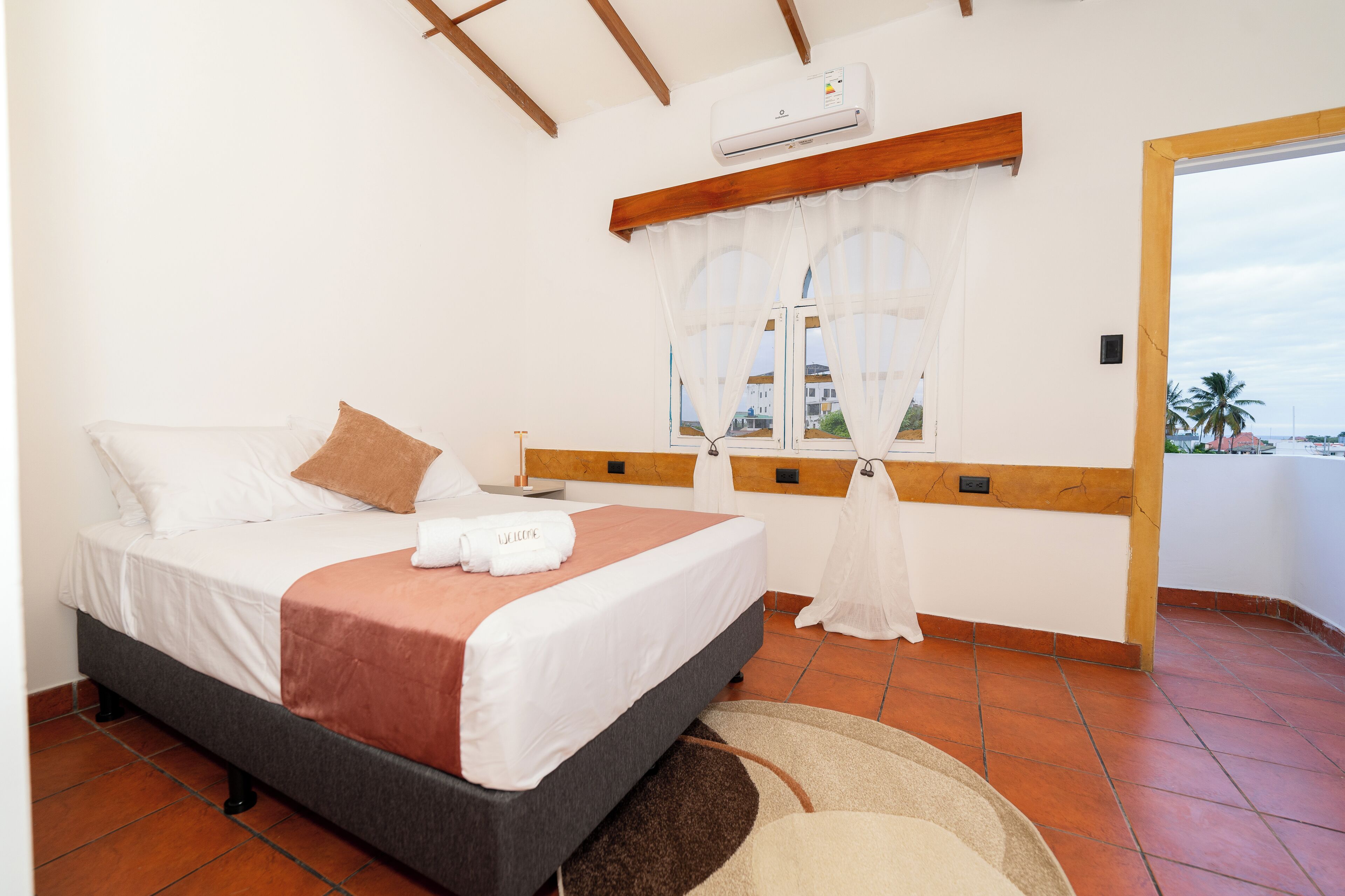 Quarto de hotel com cama, janela com cortinas, vista para o exterior e ventoinha no teto.