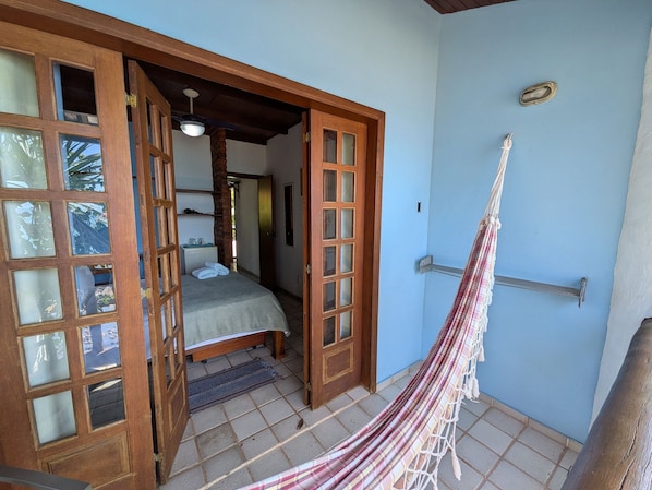 Quarto com cama, rede e porta que dá para outro cômodo.