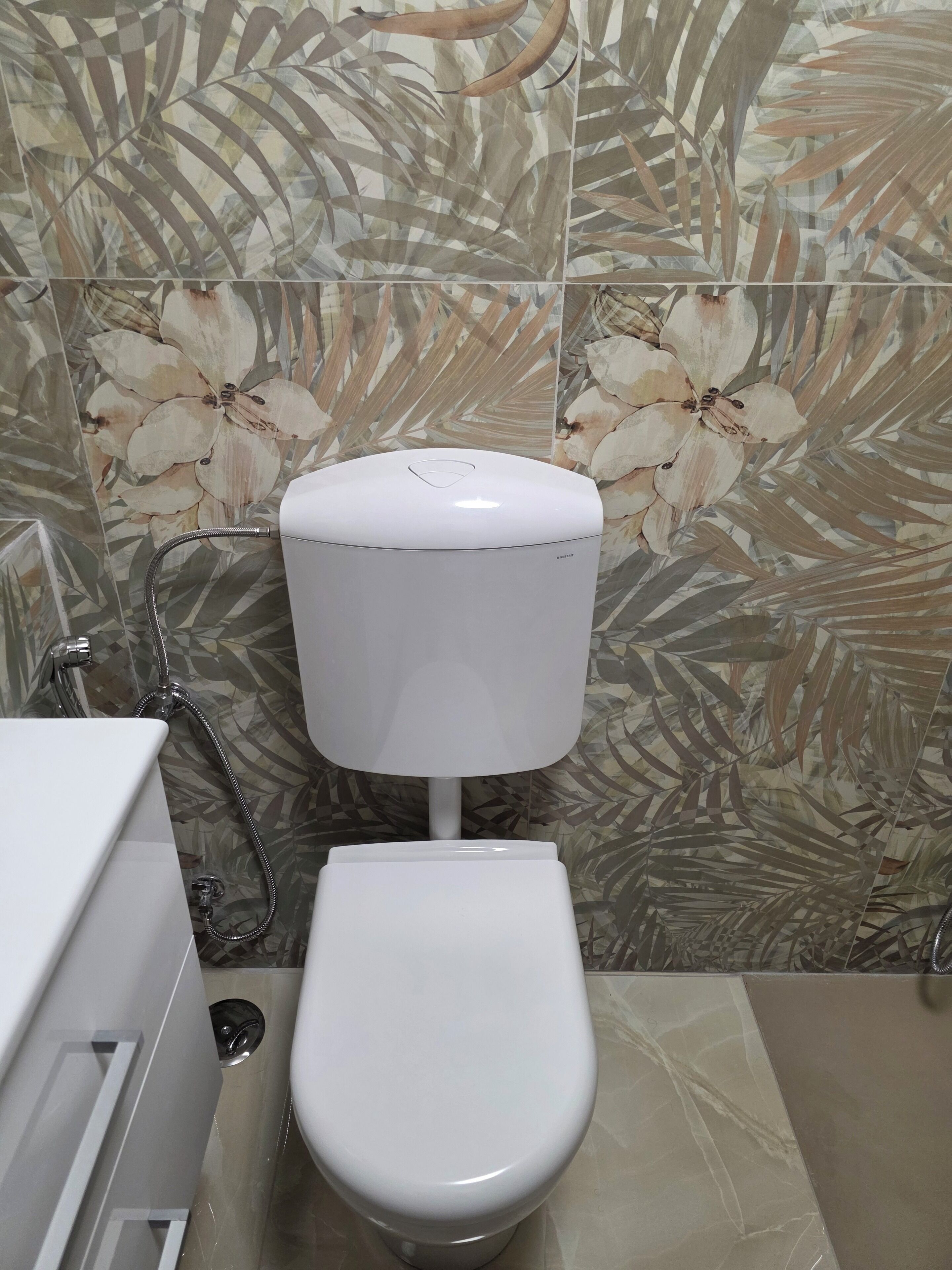 Casa de banho com sanita, lavatório e chuveiro. As paredes têm um padrão de azulejos florais.