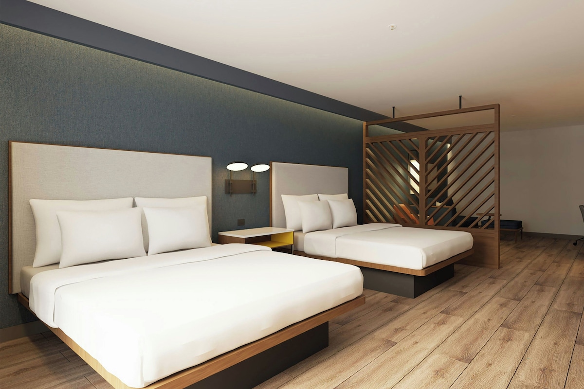 Quarto de hotel moderno com duas camas, piso de madeira, parede escura e divisória de madeira.