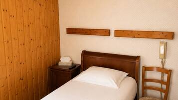 Quarto de hotel com cabeceira de madeira, mesa de cabeceira com luminária, uma cadeira e cama com edredom branco.