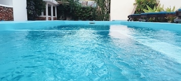 Piscina azul cristalina com um muro de pedra e vegetação ao fundo.
