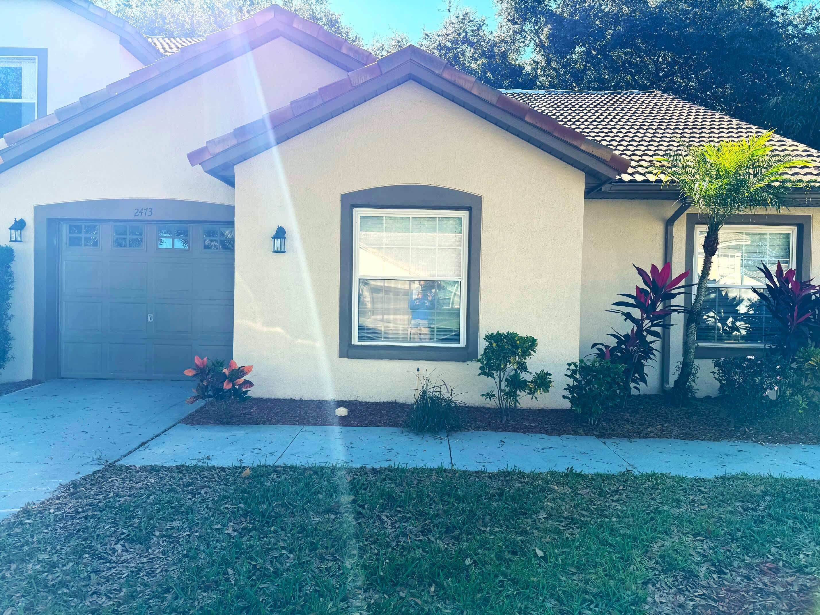 Uma casa com garagem, pequeno jardim frontal e gramado bem cuidado.