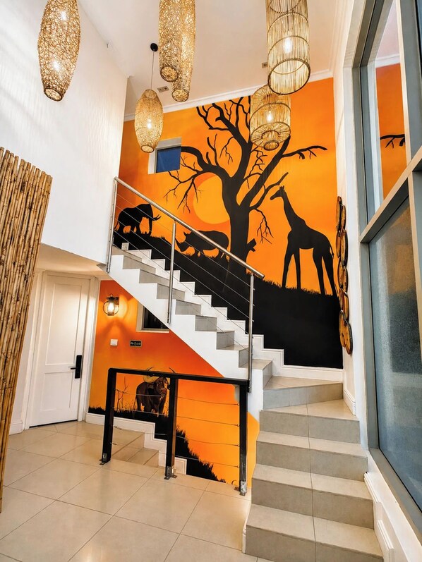 Escadaria com mural de animais e árvore, levando a um quarto com uma grande janela.